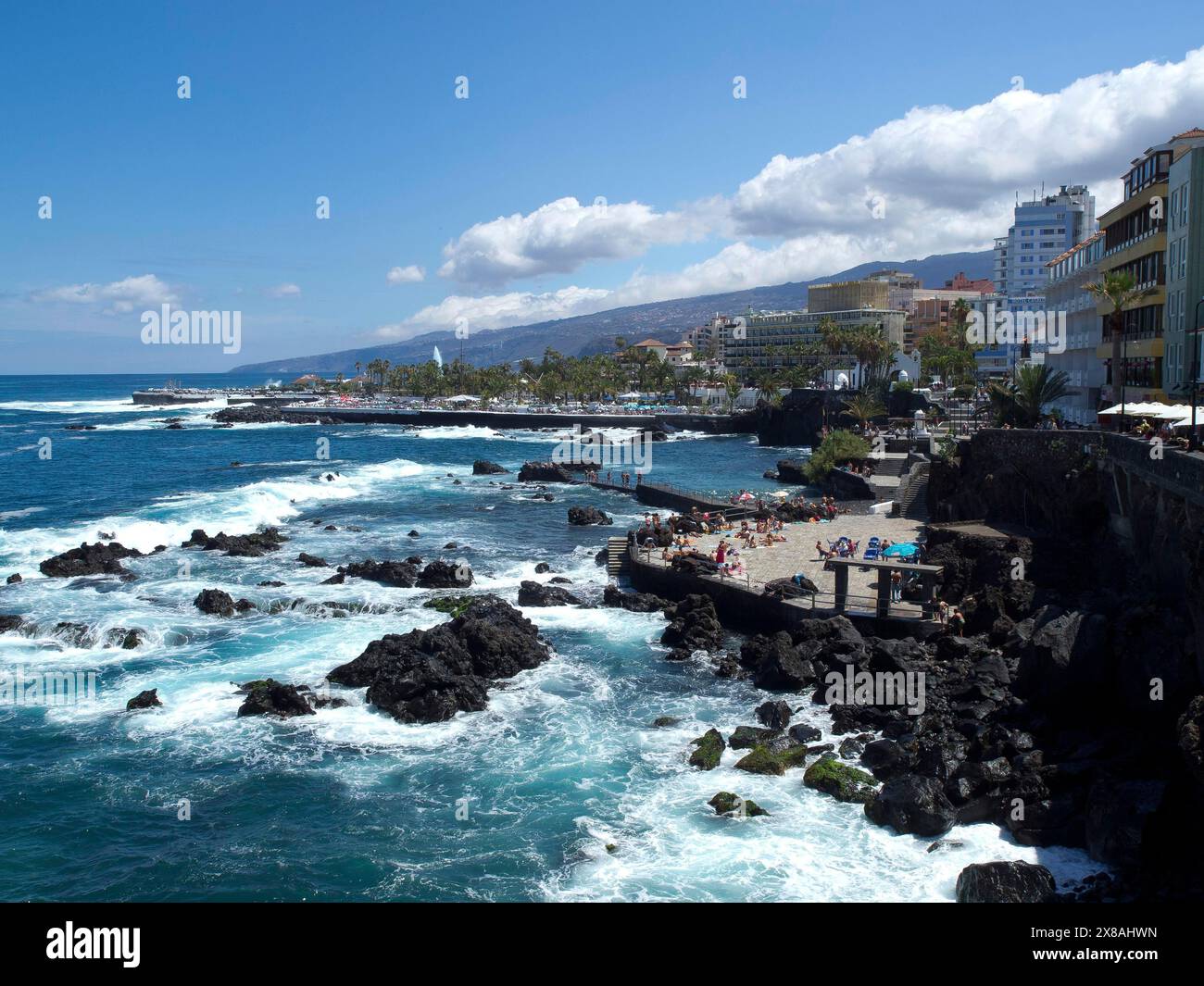 Coastal town with promenade along the rocky coast and waves hitting the ...