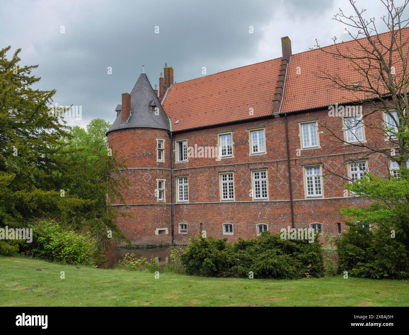 Large brick building with roof and tower, surrounded by green hedge and ...