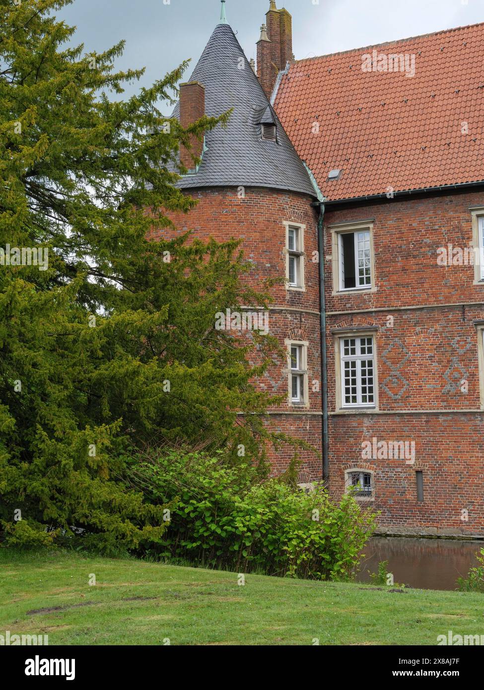 Brick building with tower and pointed roof, surrounded by tall trees ...