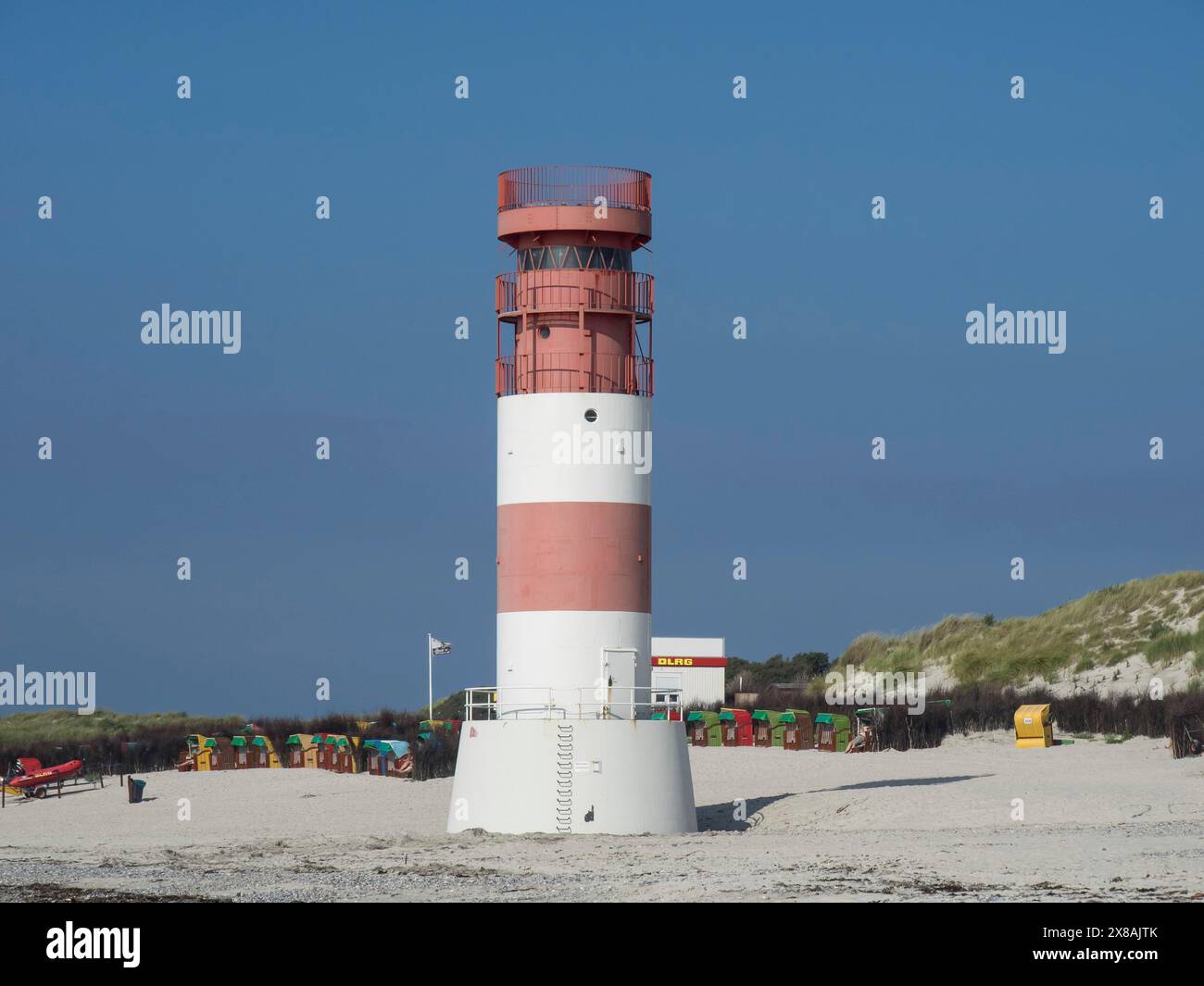 Red and white lighthouse in front of some deckchairs on a sandy beach ...