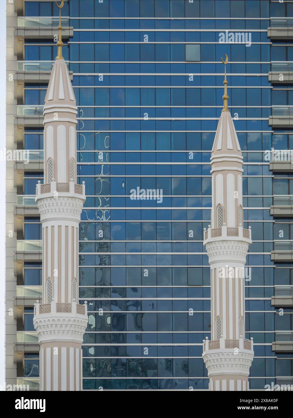 Two minarets of a mosque in front of a modern building with glass ...