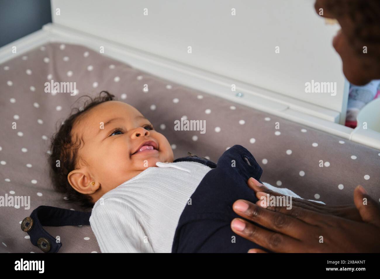 Baby laughs while is being dressed up by her mom on a changing table ...