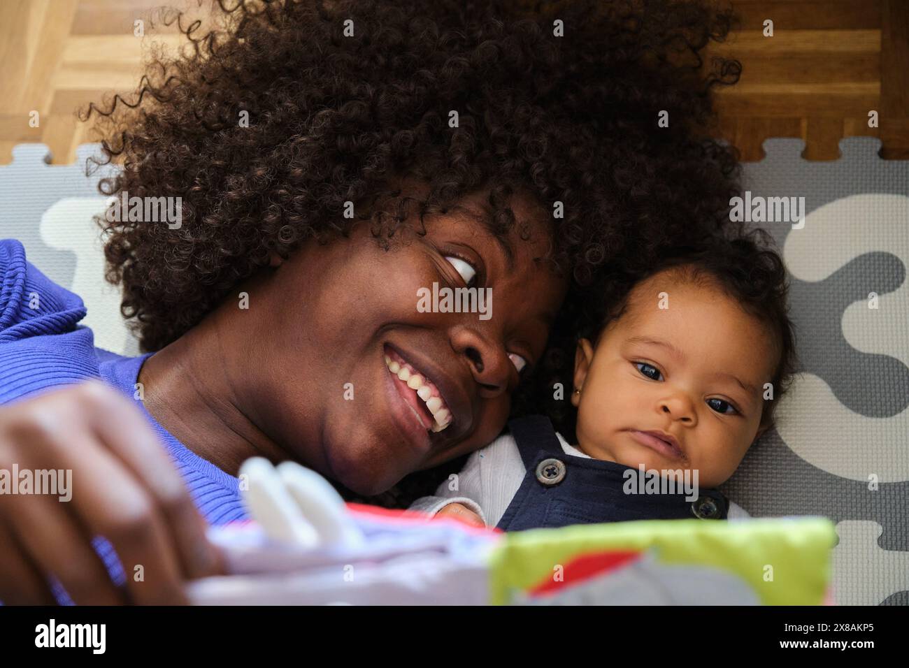 African woman is laying on the floor with a baby reading a book Stock ...