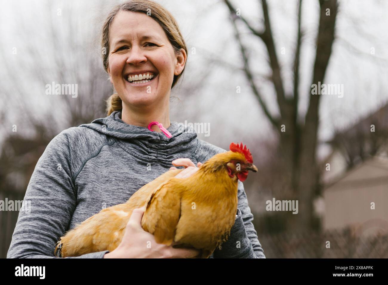 Middle aged woman holds a golden chicken outside with trees Stock Photo ...