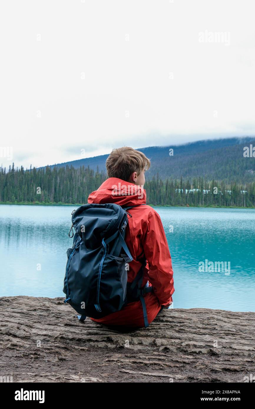 A tween boy wearing a backpack sits on a rock overlooking Emeral Stock ...