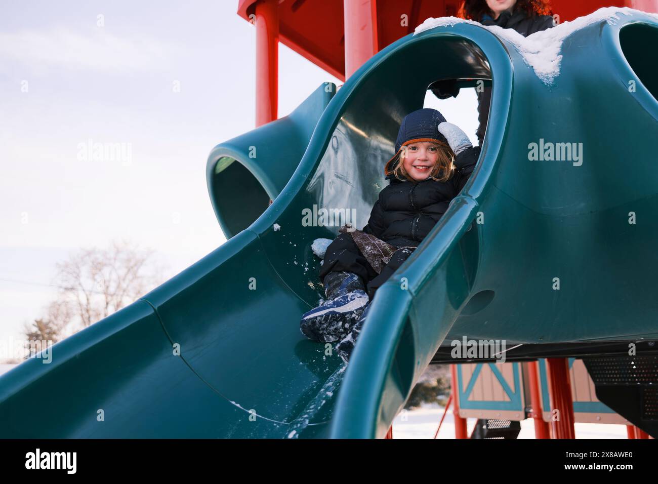 Smiling child sliding down a playground slide in winter Stock Photo - Alamy