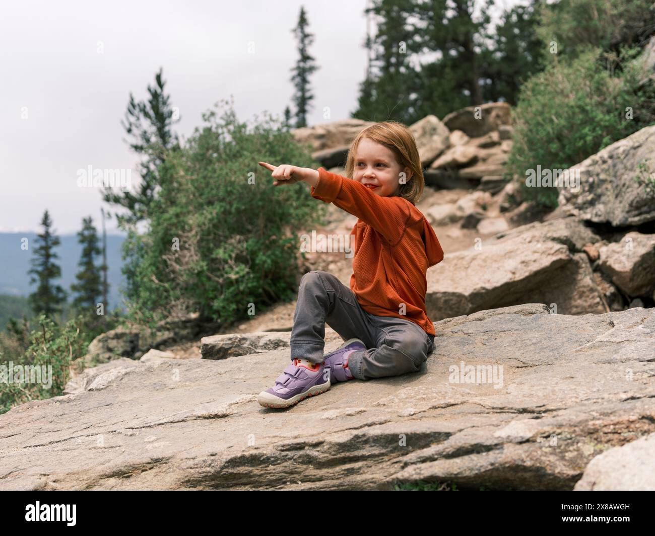 Child sitting on a rock pointing in the distance during a hike Stock ...