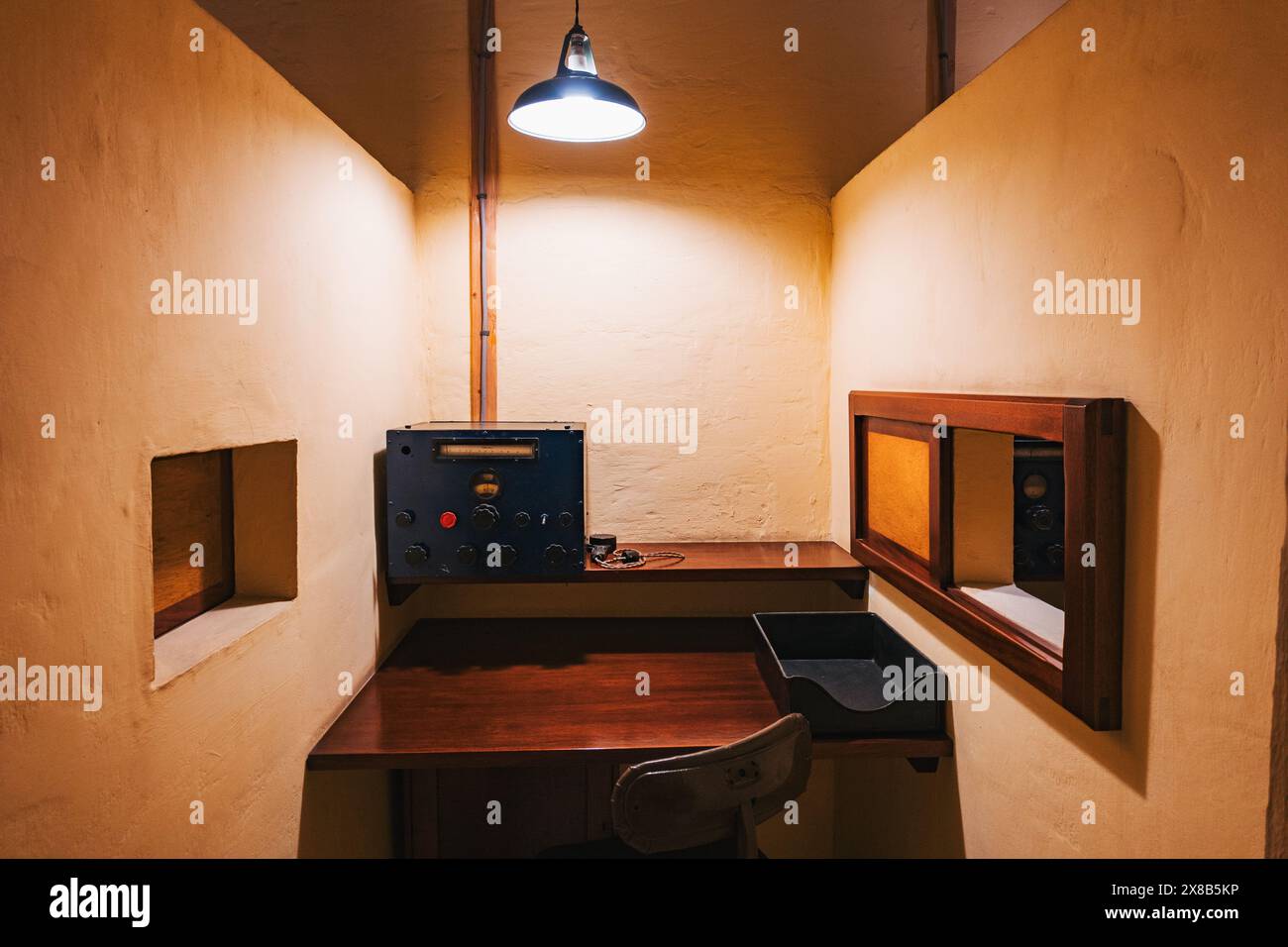 A small room with a desk, a chair, and an old radio transceiver. A ...