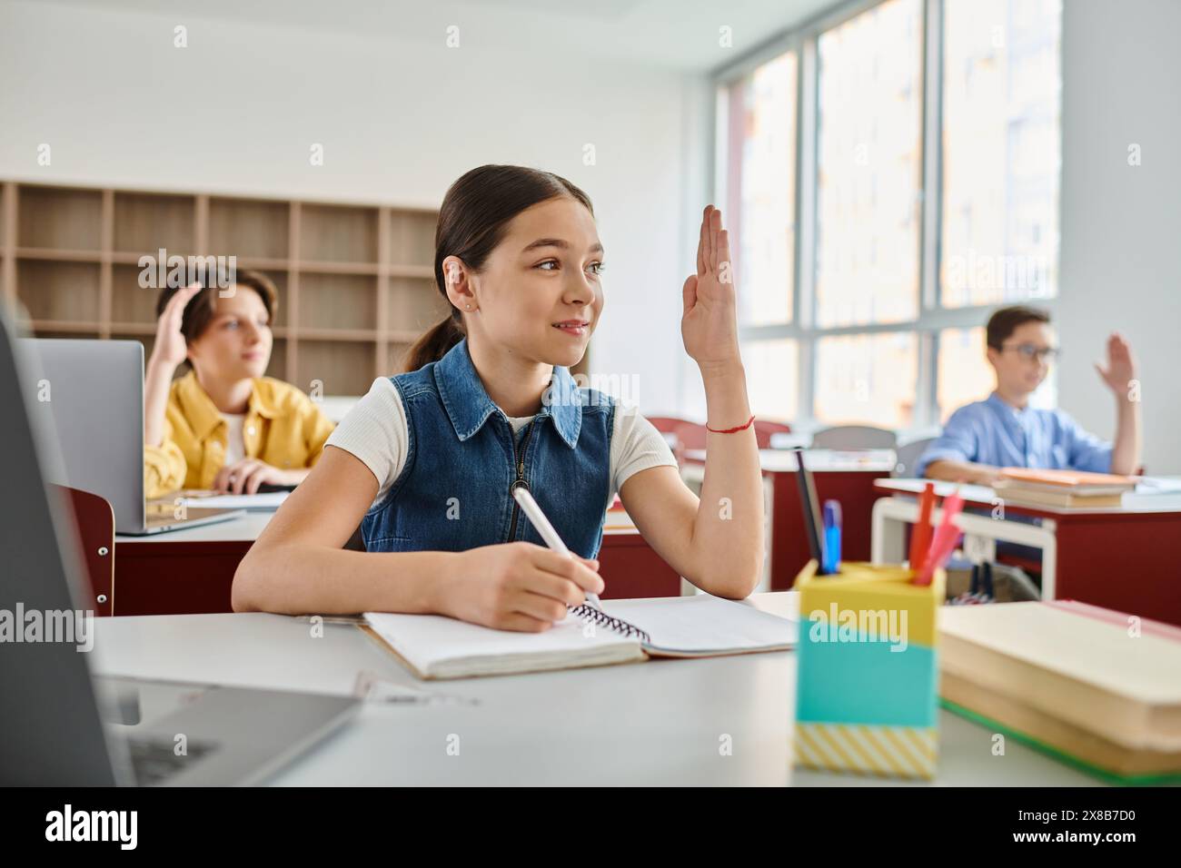 A young girl with a curious expression sits at a desk in front of a ...