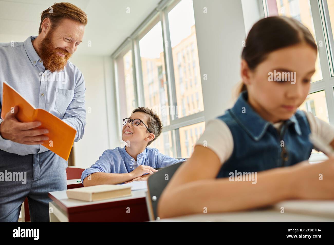 A male teacher stands next to a student in a lively classroom ...
