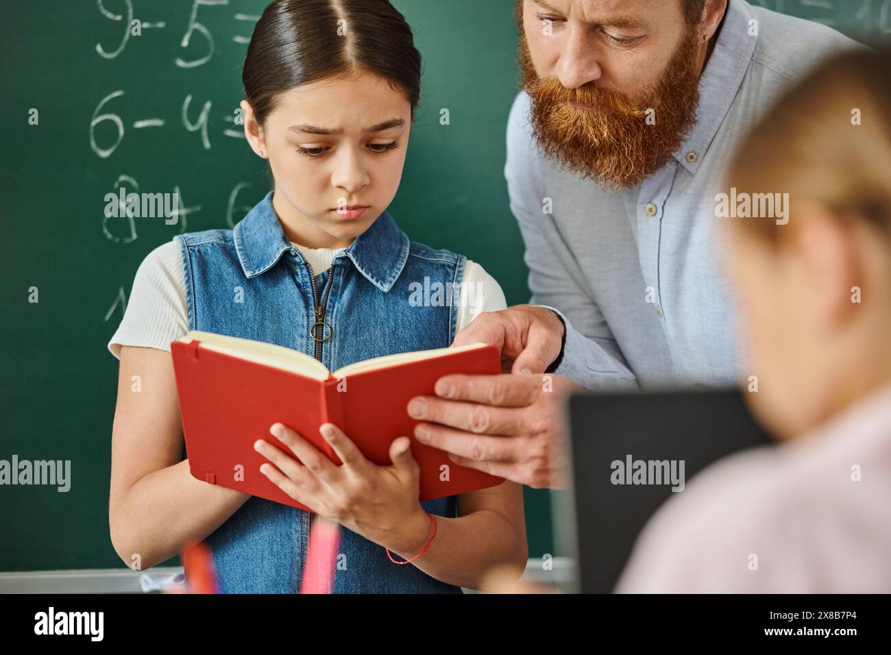 A man teacher reading a book to a young girl with an interested ...