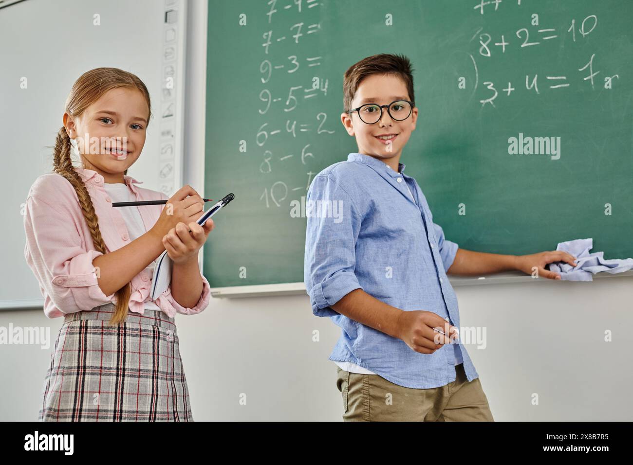 boy and girl stand in front of a blackboard, eager to learn in a bright ...