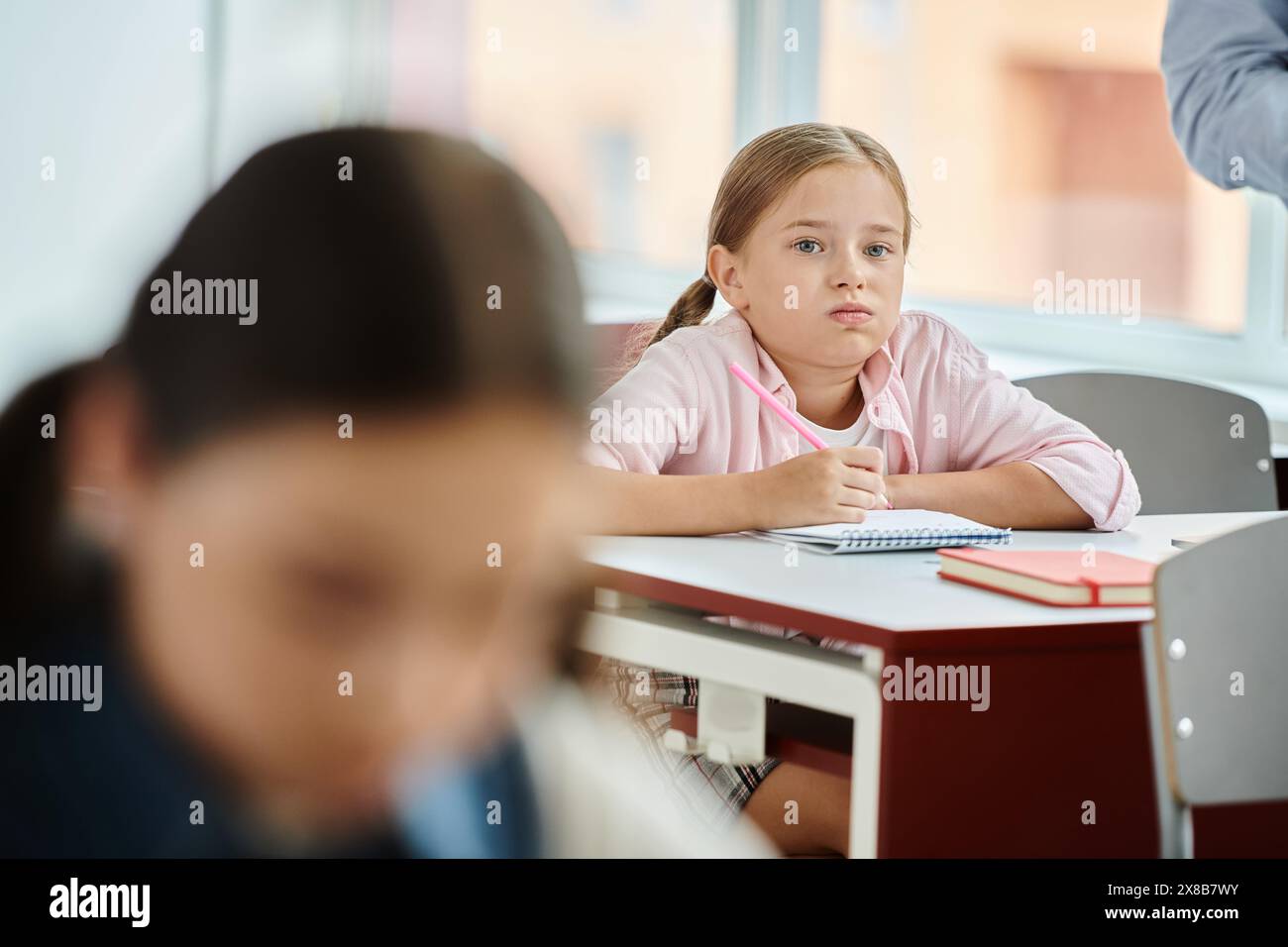A young girl with pigtails sits at her desk, listening to the teachers ...