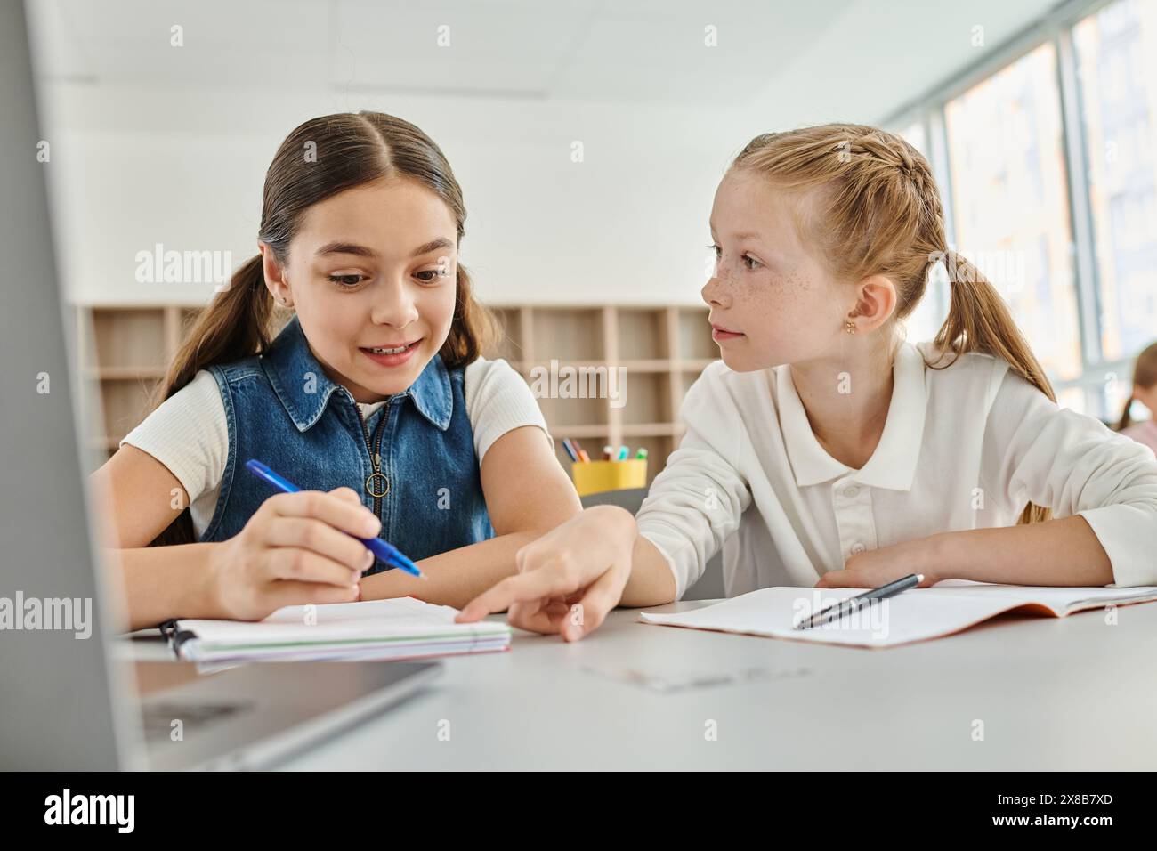 Two young girls with focused expressions sitting at a desk, diligently ...