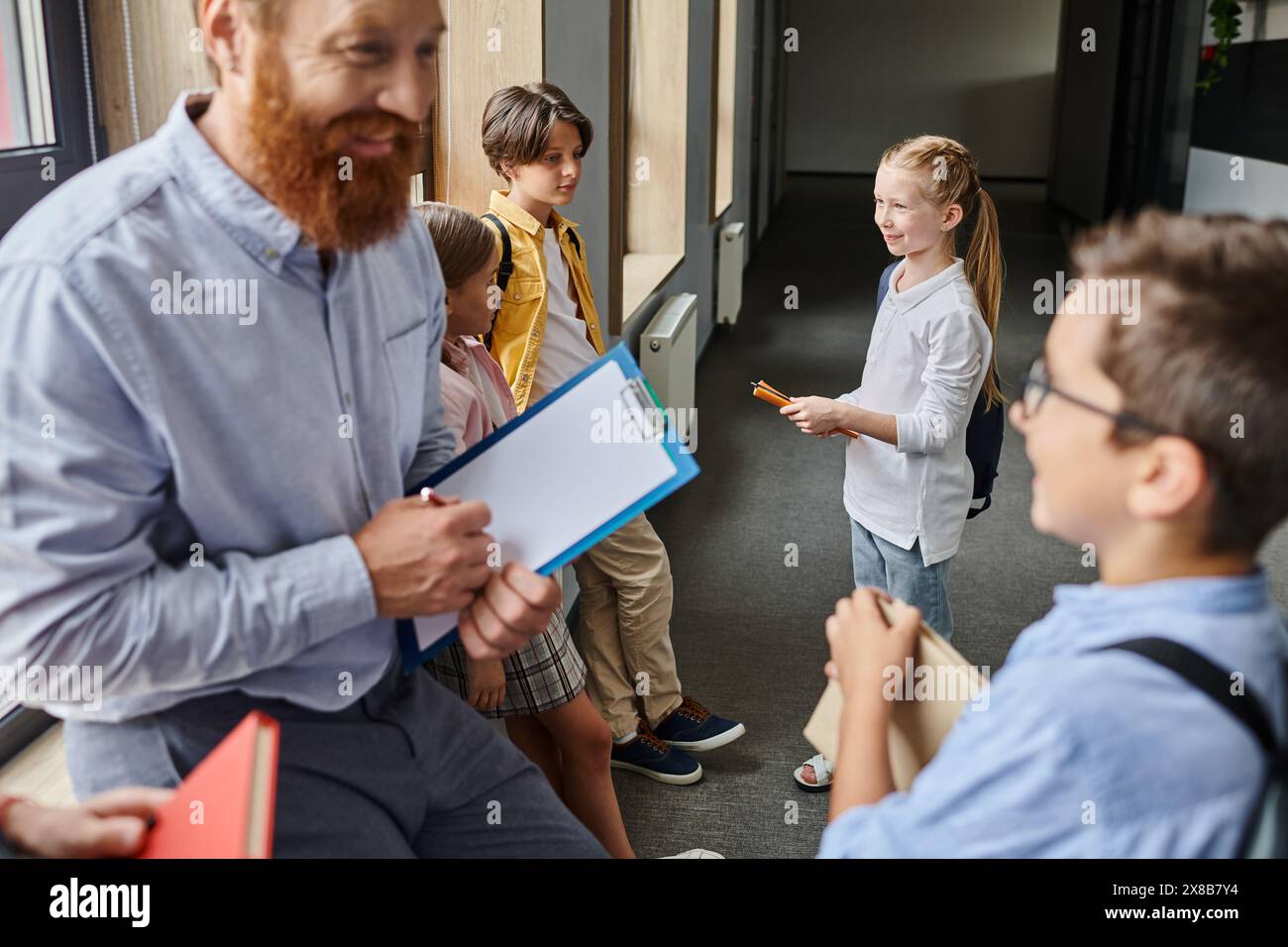 A male teacher holding a clipboard stands beside a group of kids in a ...