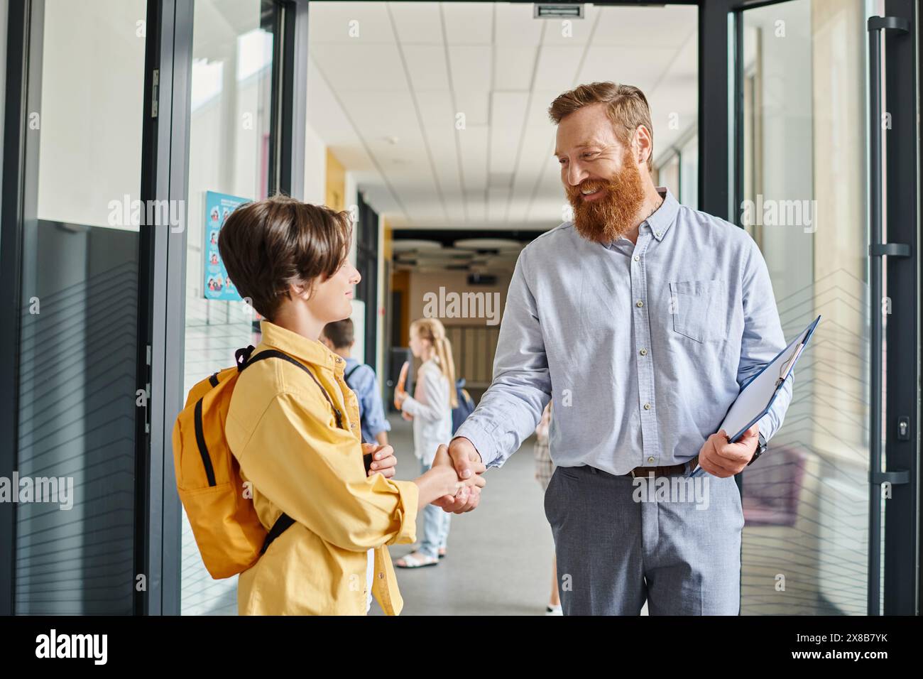 A man in a classroom setting, shaking hands with a young boy ...