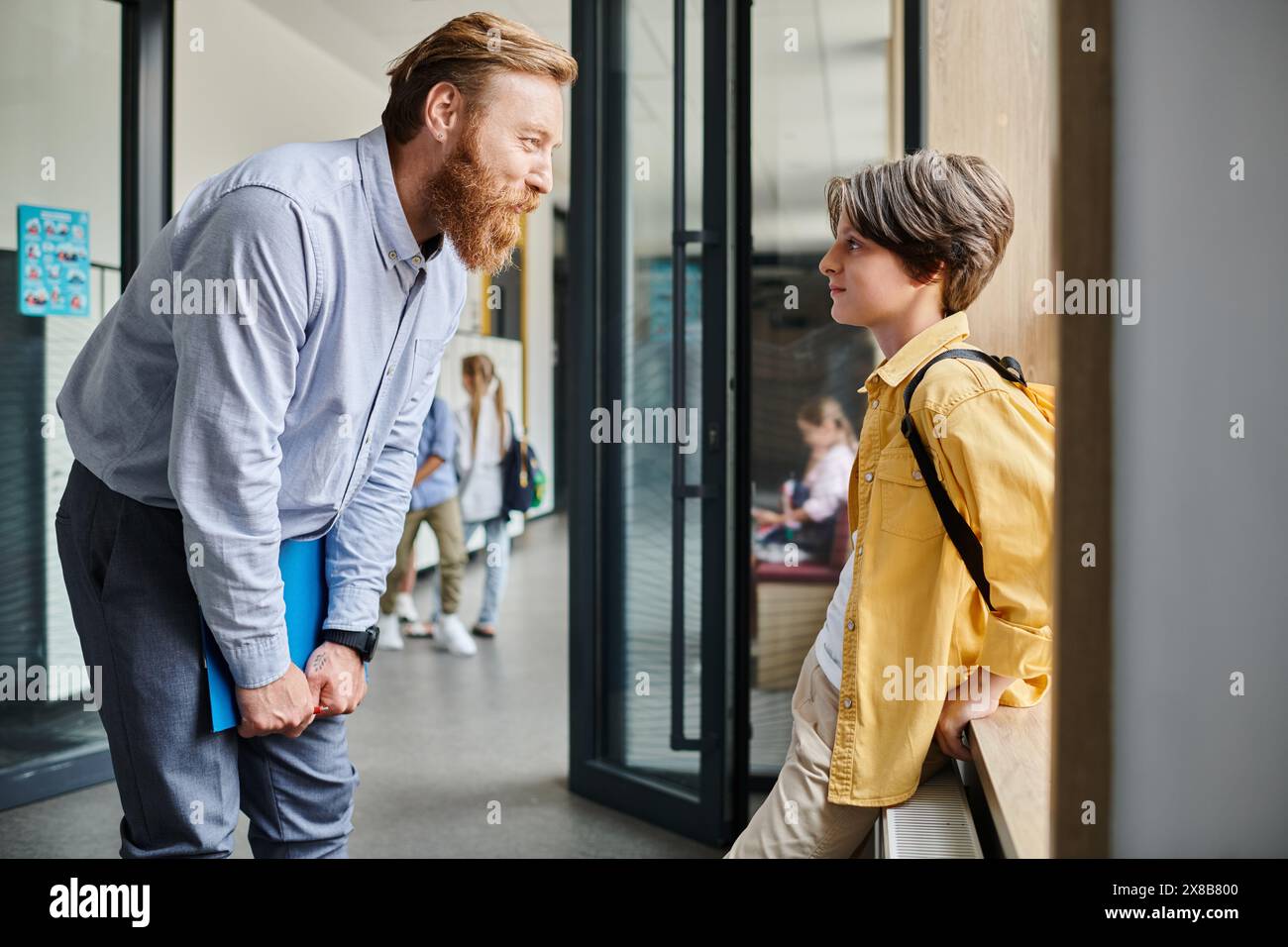 A man stands next to a little boy in a bright classroom, offering ...