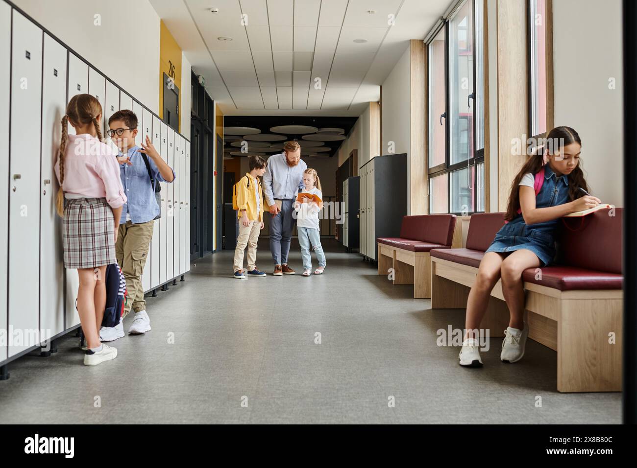 group of children stand in hallway beside lockers while a teacher ...