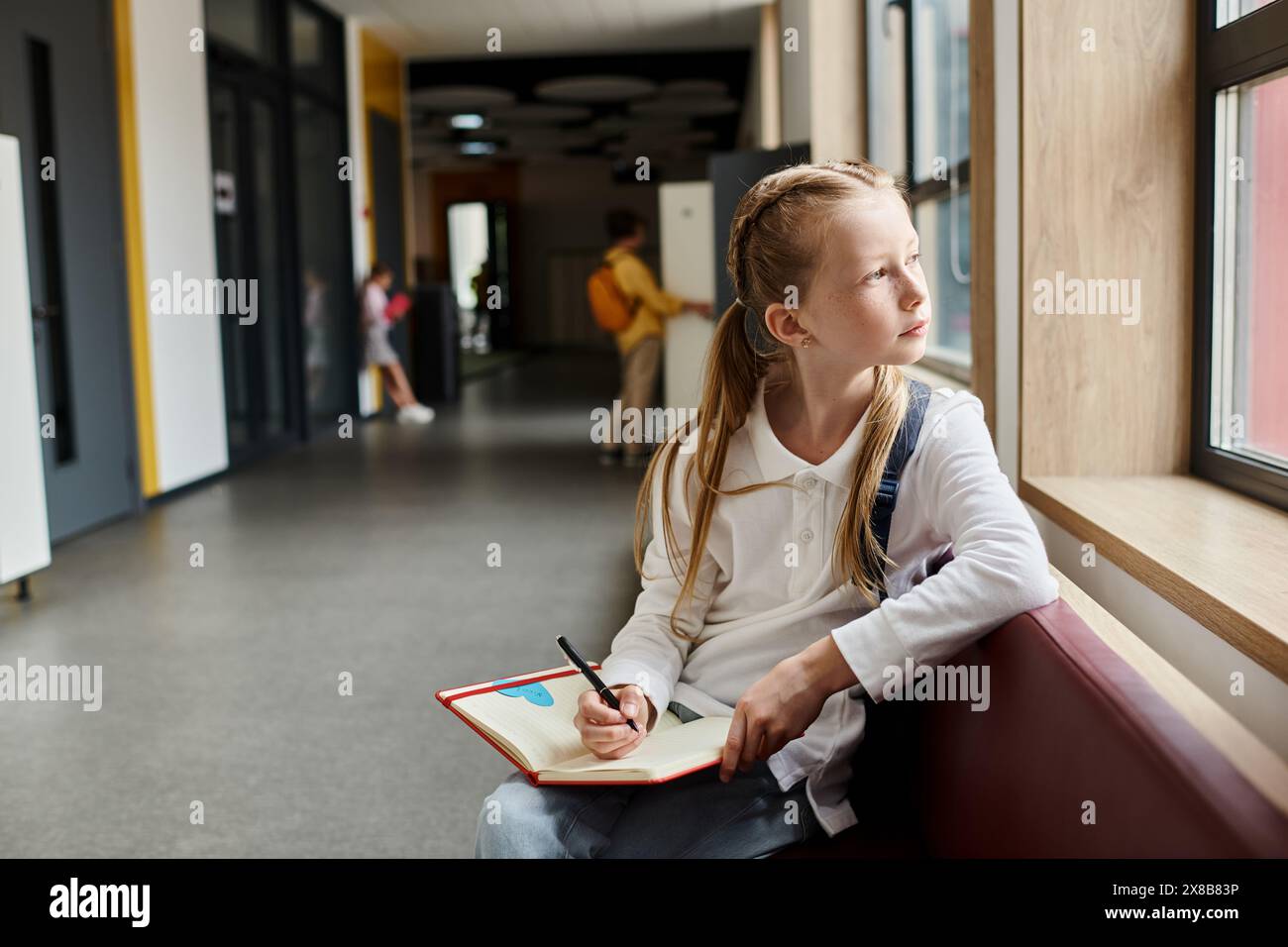 A young girl with a focused expression sits on a window sill, writing ...
