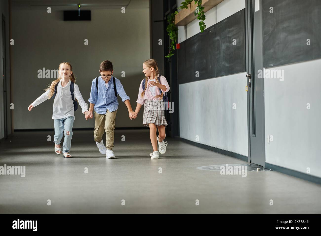 A group of children, walking down a brightly lit hallway in a school ...