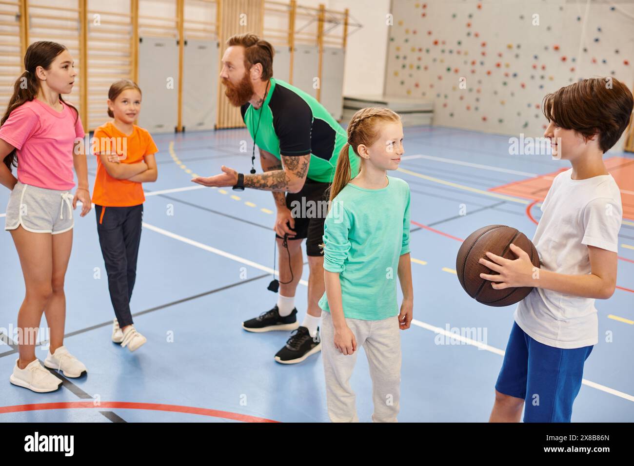 group of people, led by a male teacher, standing around in a gym ...