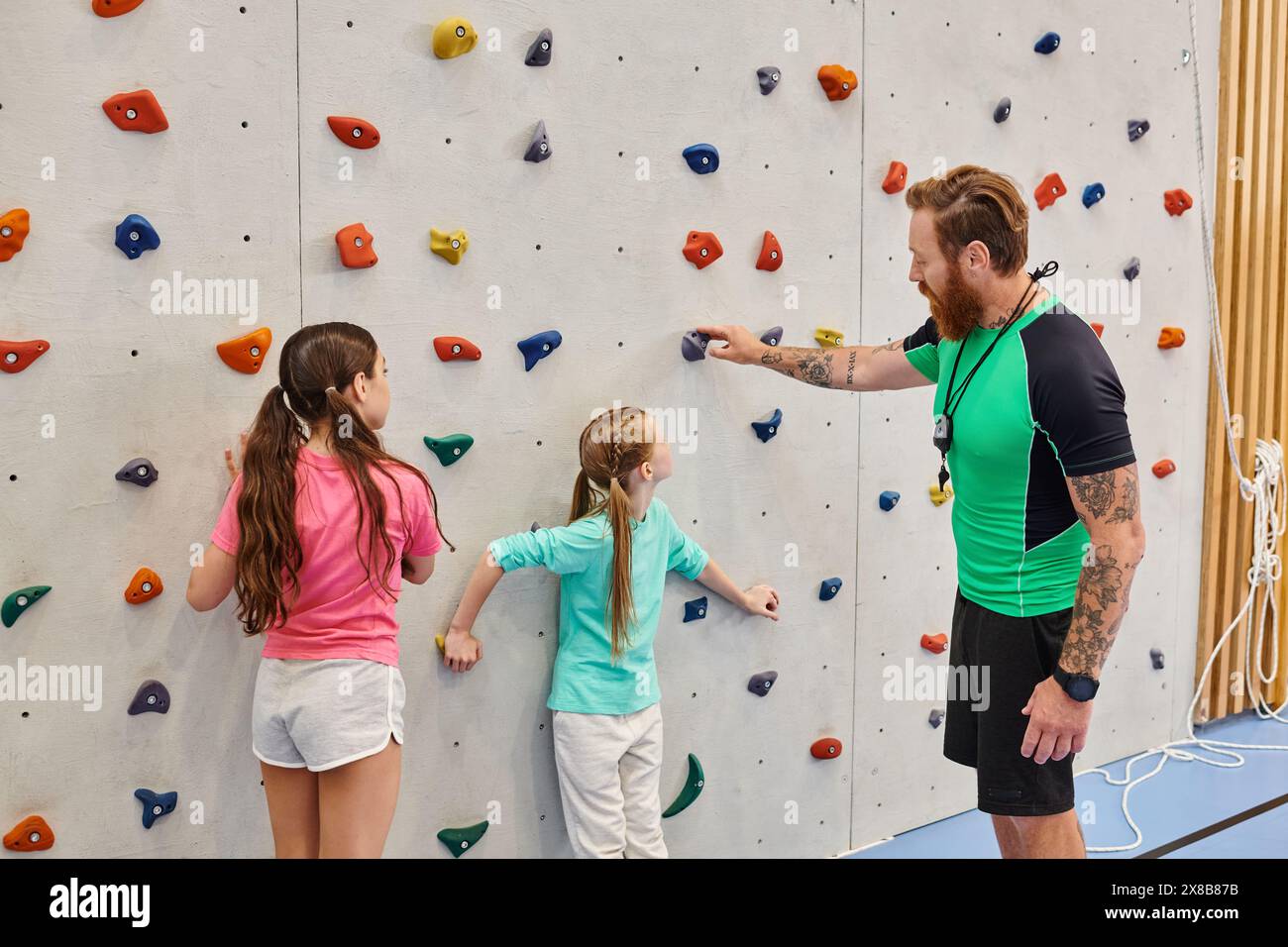 A man teacher instructs two young girls in front of a climbing wall in ...