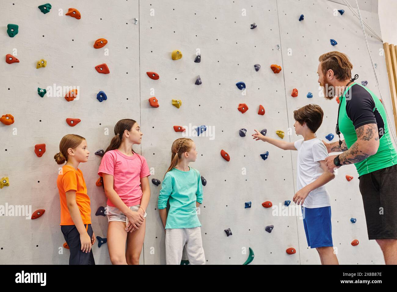 A man teaches a group of diverse children how to climb on a rock wall ...