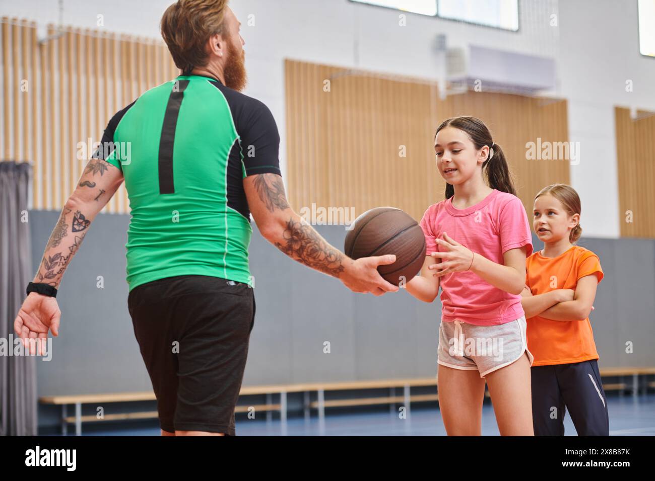 A male teacher stands holding a basketball in front of a diverse group ...