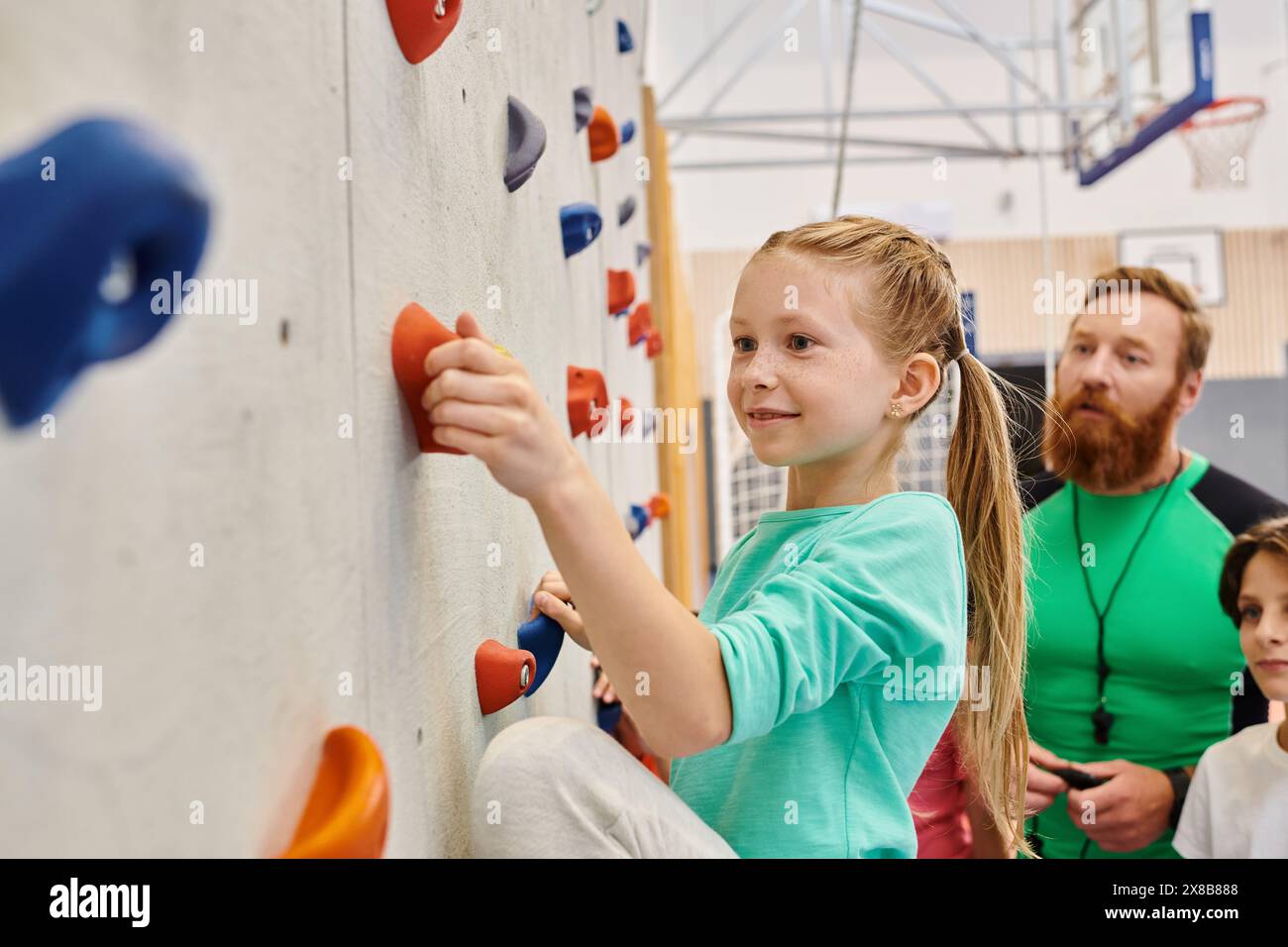 teacher and children, gathered around a colorful climbing wall ...