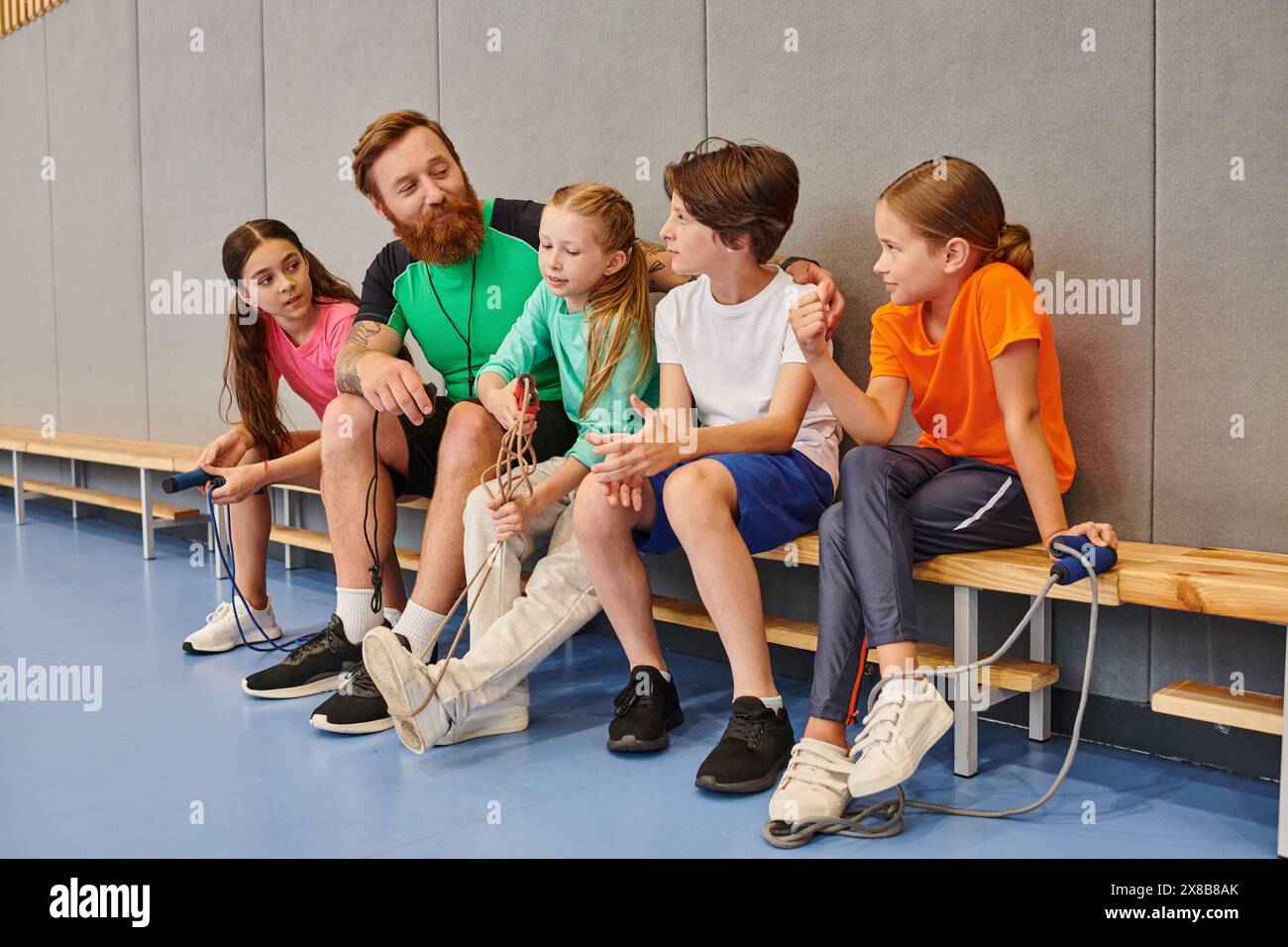 A group of diverse kids sit closely together on a bench, listening ...