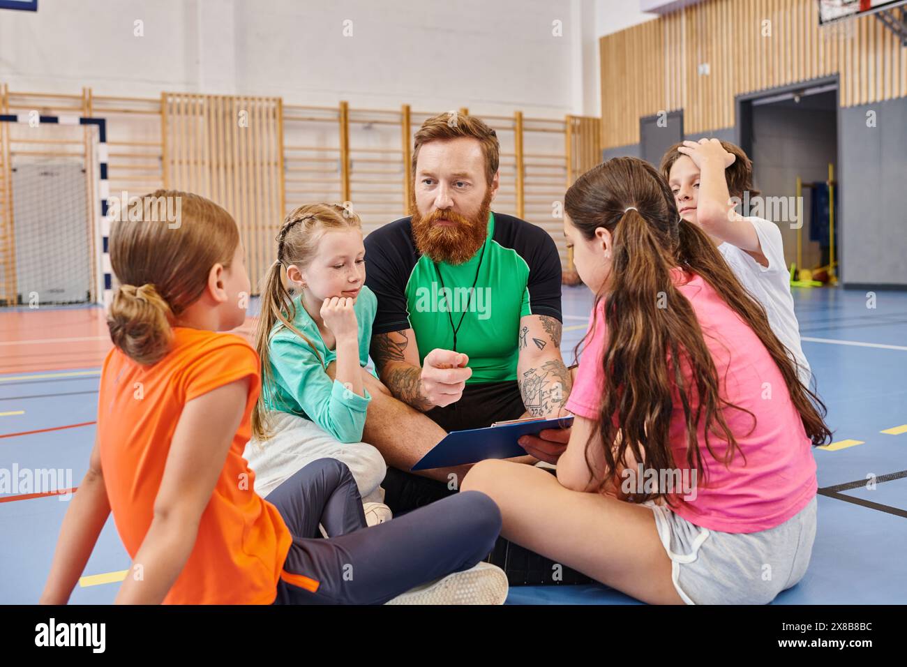 A male teacher sits on the floor surrounded by a diverse group of children in a bright and ...