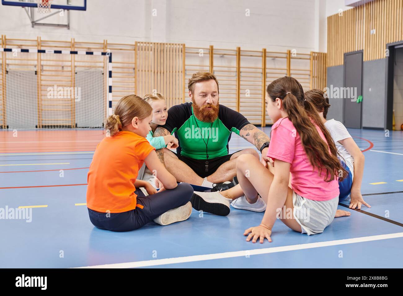A male teacher sits on the floor surrounded by a diverse group of ...