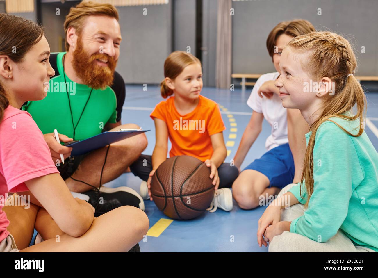 A diverse group of children sit attentively around a basketball as ...