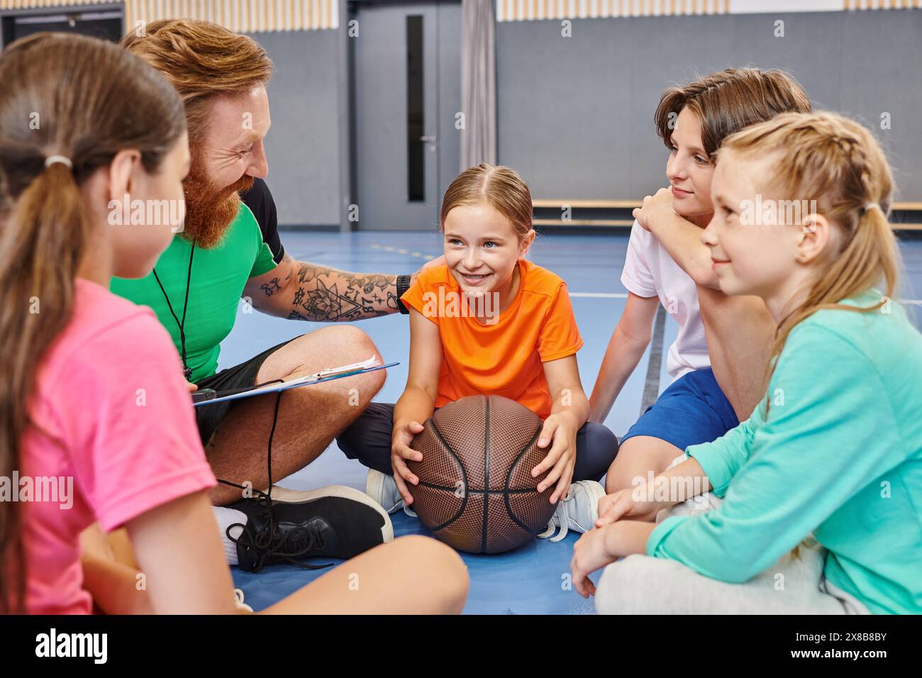 A man teacher with a diverse group of kids sitting around a basketball ...