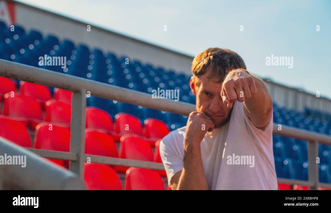 A man is standing in front of a row of red and blue seats, practicing ...