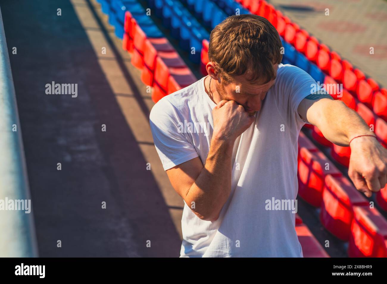 A man is standing in front of a row of red and blue seats, practicing ...