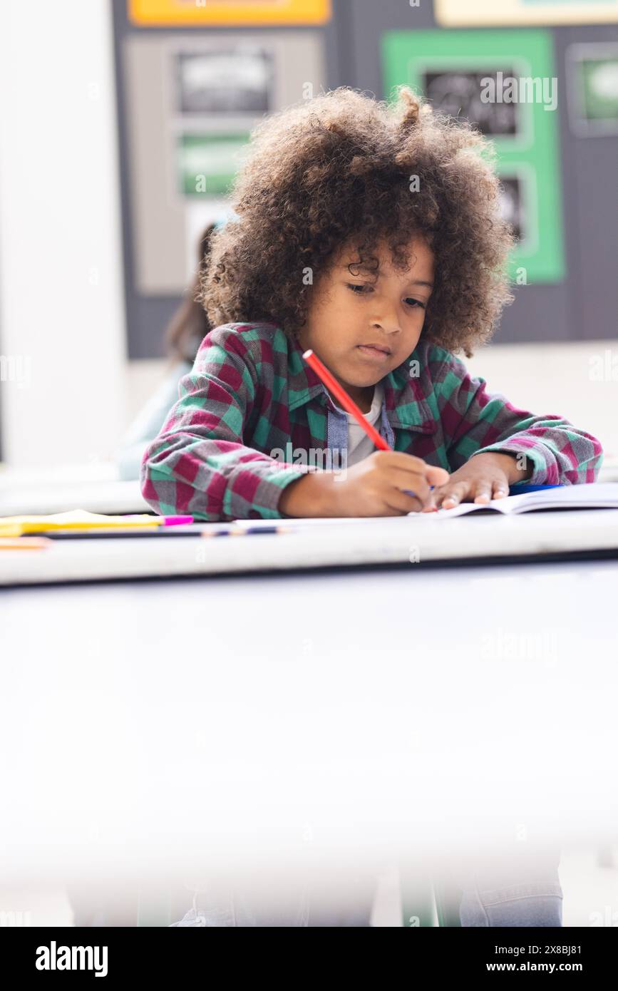 In school, in classroom, young biracial boy focusing on writing ...