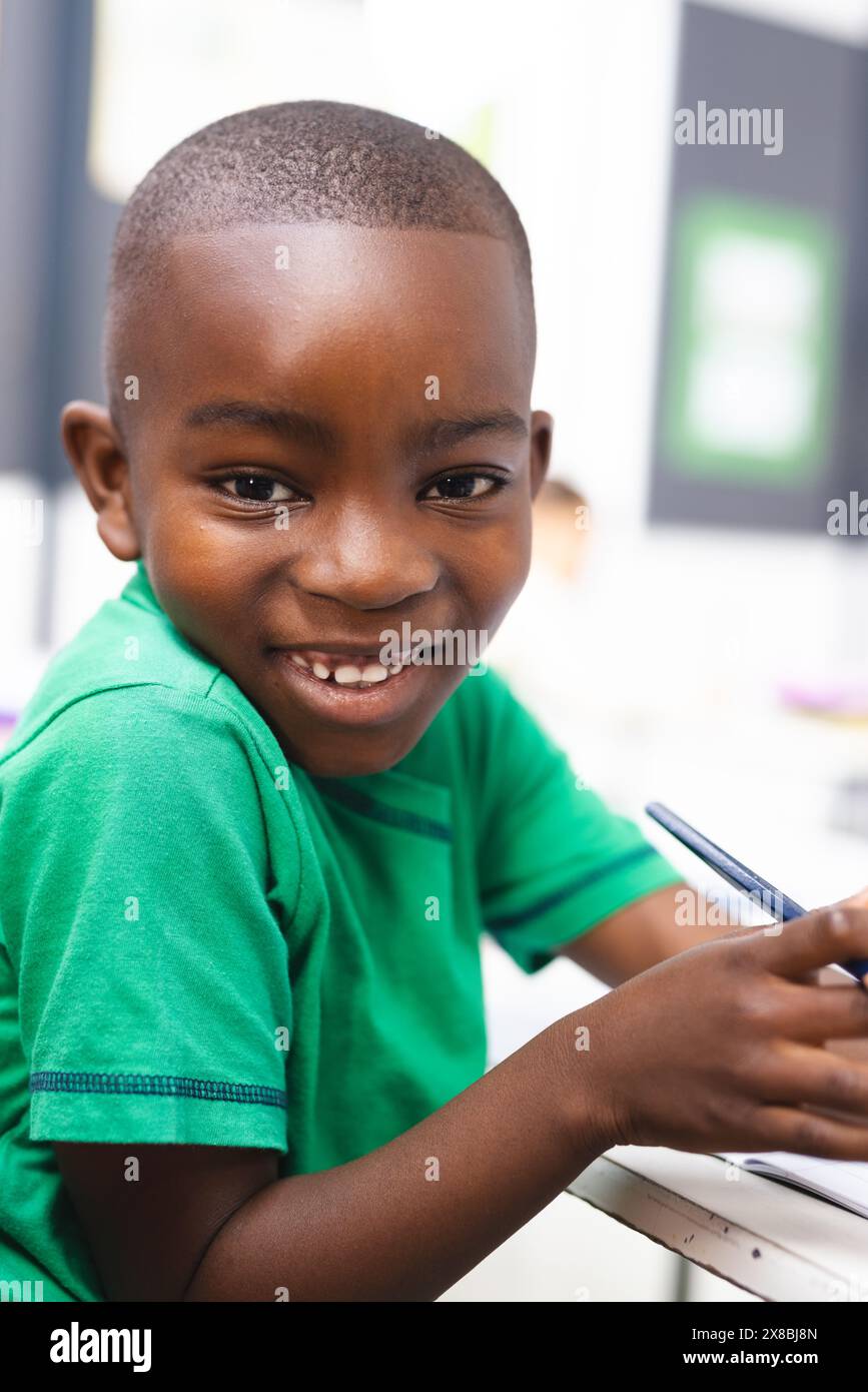 In school, young African American boy wearing a green shirt is writing ...