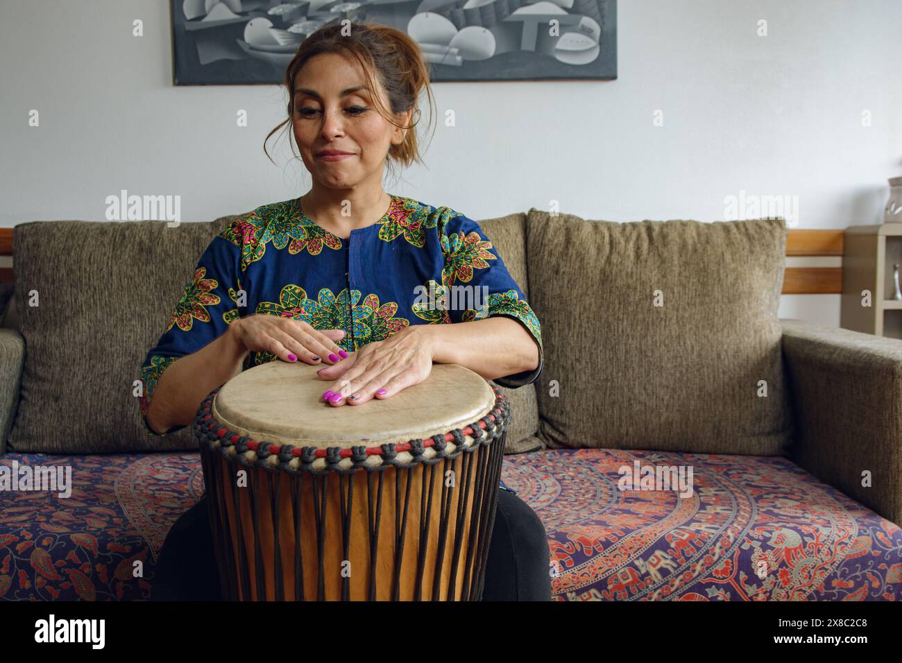 A Latin happy Adult Woman at home is sitting on a couch and playing a ...