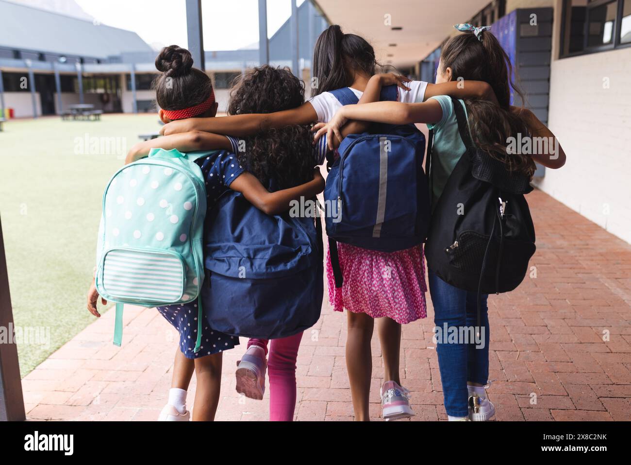 In school, four young girls are walking together outdoors, hugging each ...
