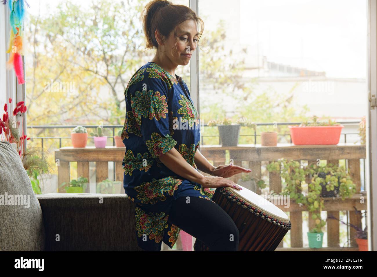 Side view of an Adult Woman sitting at home playing Djembe drum ...