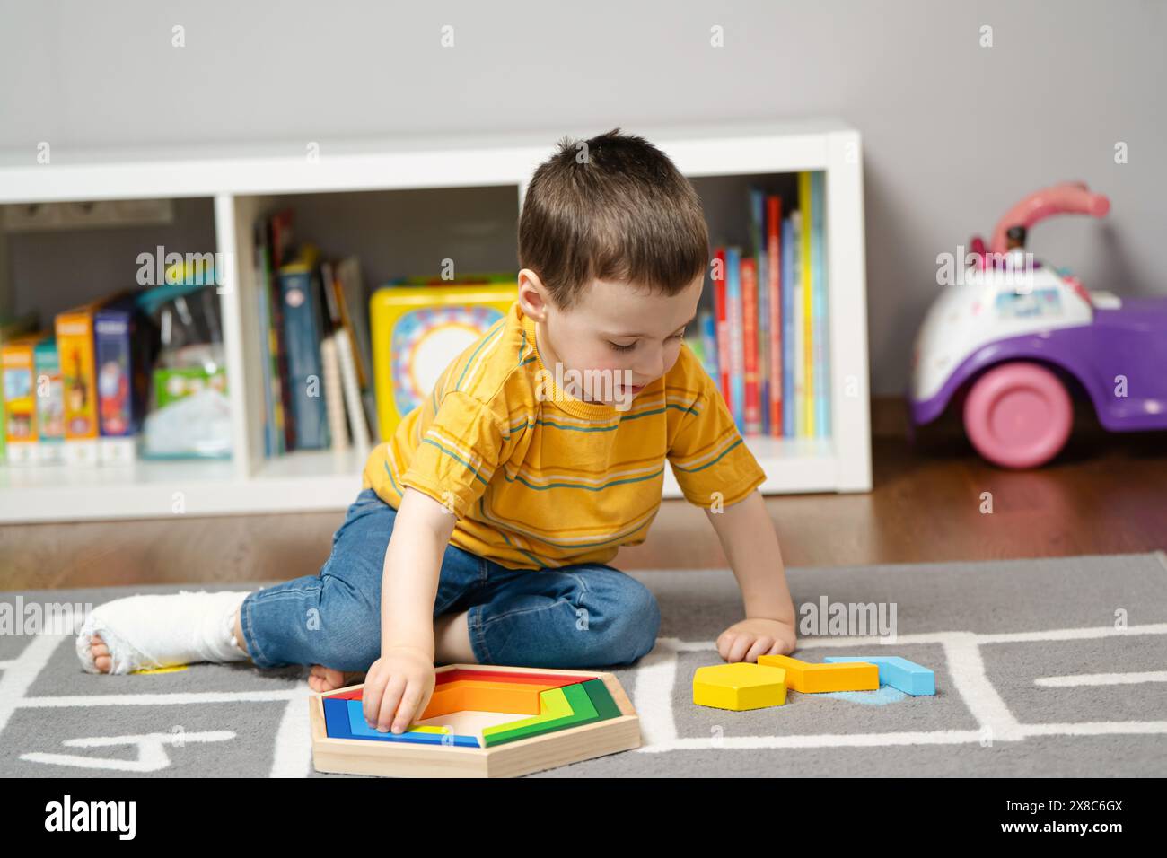 Toddler boy with a bandage or cast on his leg plays with wooden blocks ...