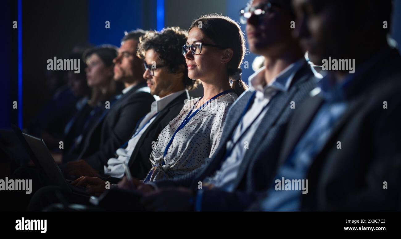 Female Sitting in a Dark Crowded Auditorium at a Tech Conference. Young Woman Using Laptop ...