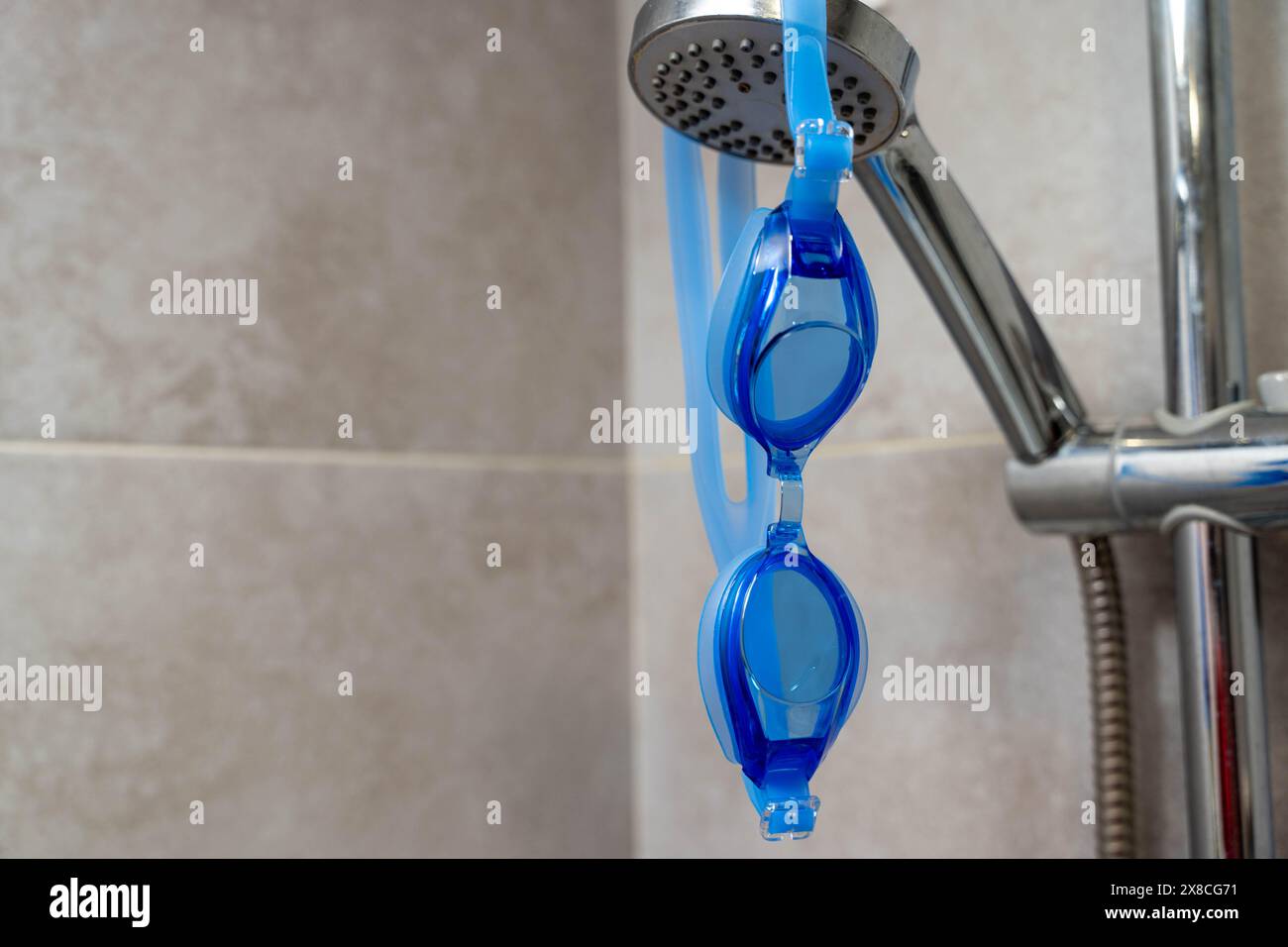 A pair of blue and yellow swimming goggles hanging on a metal hook in a ...