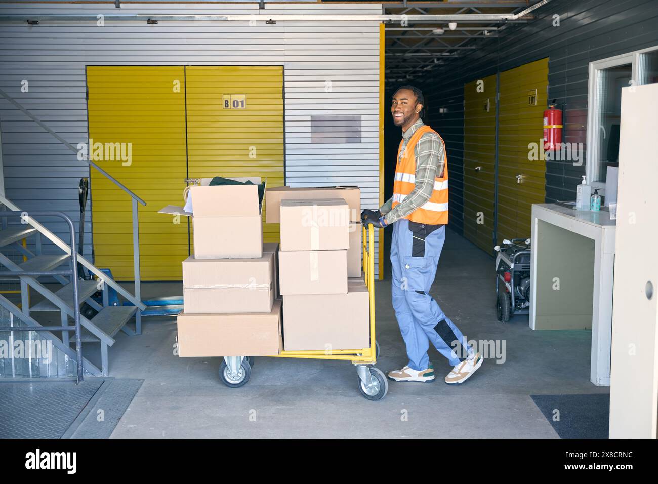 Freight handler transporting goods on wheeled cart in warehouse Stock ...