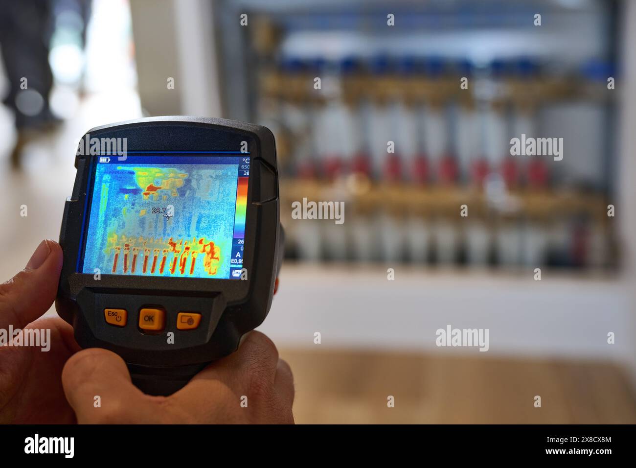 The image depicts a handheld thermal camera being used to measure the ...