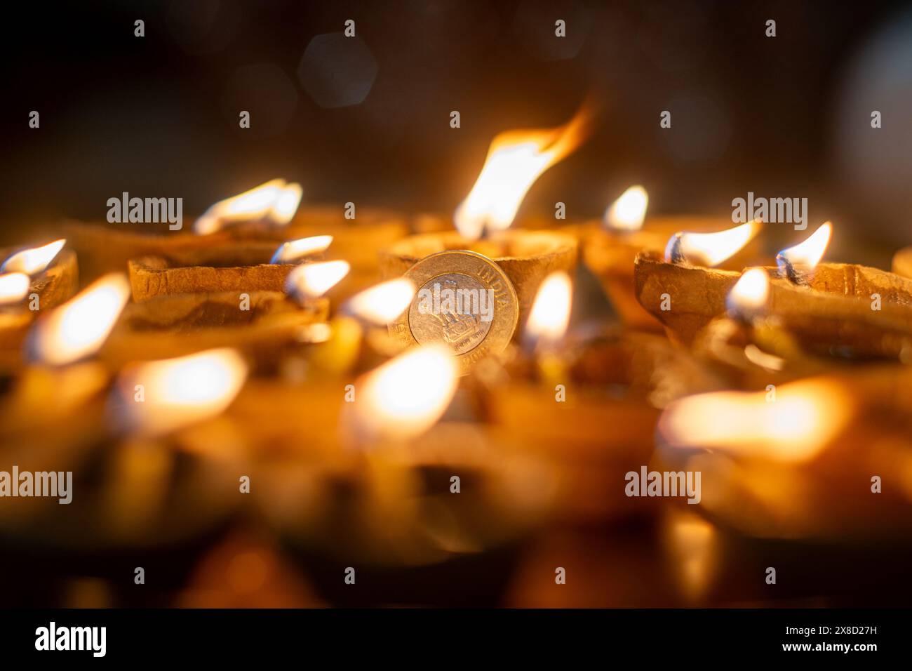 macro shot showing a circle of diya oil lamps around a rupee coin ...