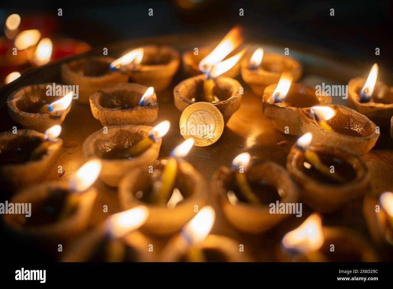 macro shot showing a circle of diya oil lamps around a rupee coin ...