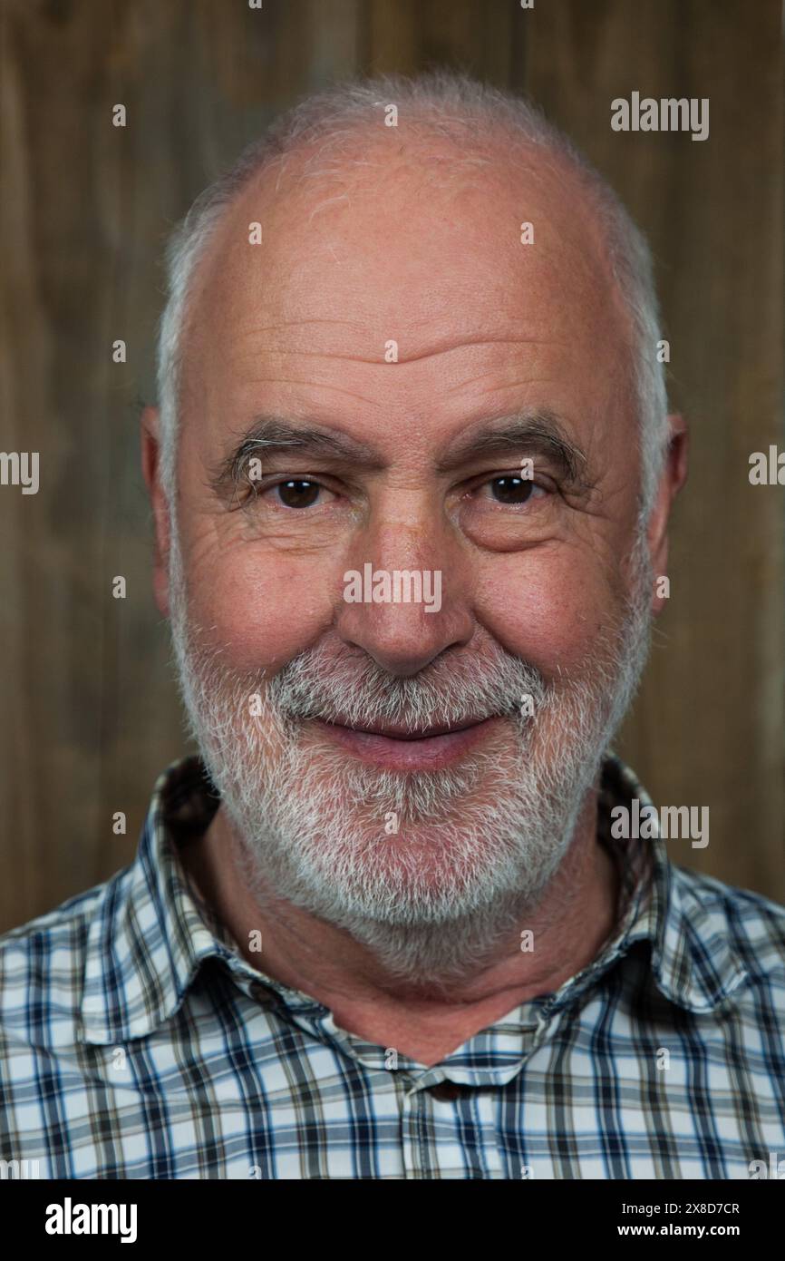 An older man with gray hair and a gray beard smiles warmly at the ...