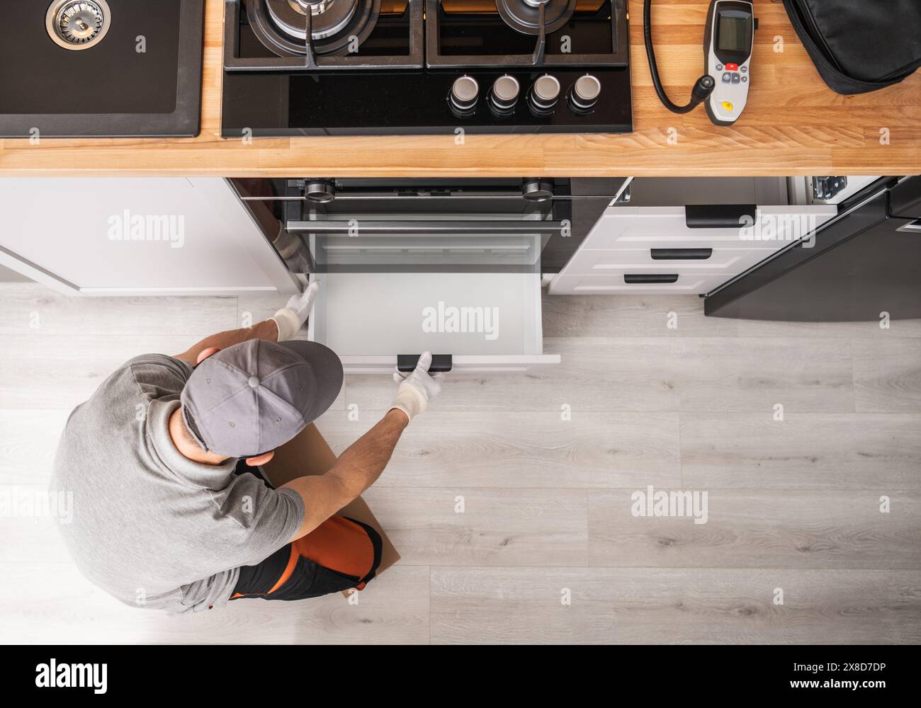 A man wearing work clothes is focused on fixing a stove in a modern ...